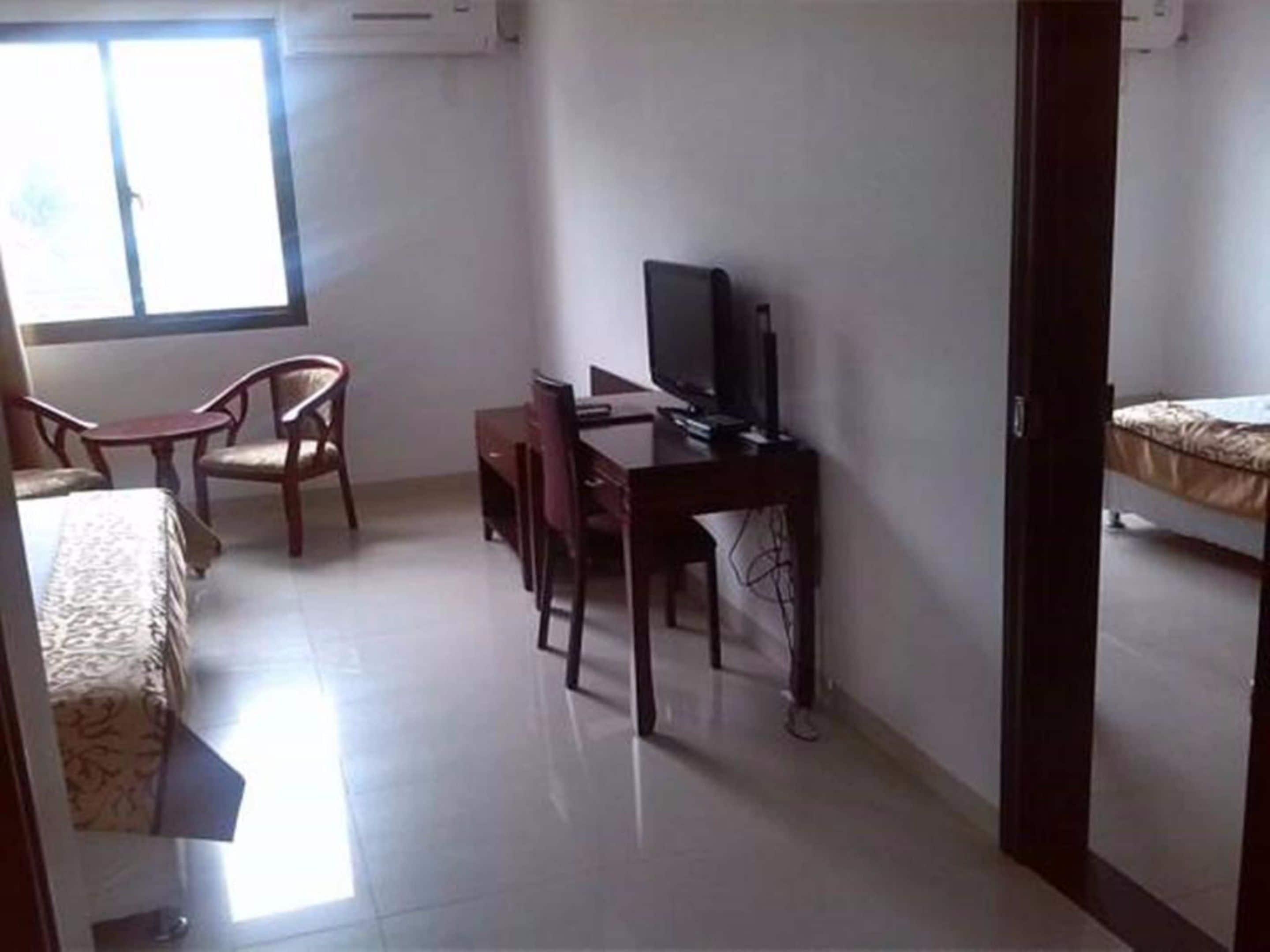 Quarto com cama, escrivaninha com televisão, cadeira e janela.