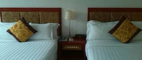 Quarto de hotel com duas camas, cada uma com cabeceira e almofada estampada com padrão floral. Um criado-mudo entre as camas possui uma luminária e um telefone.