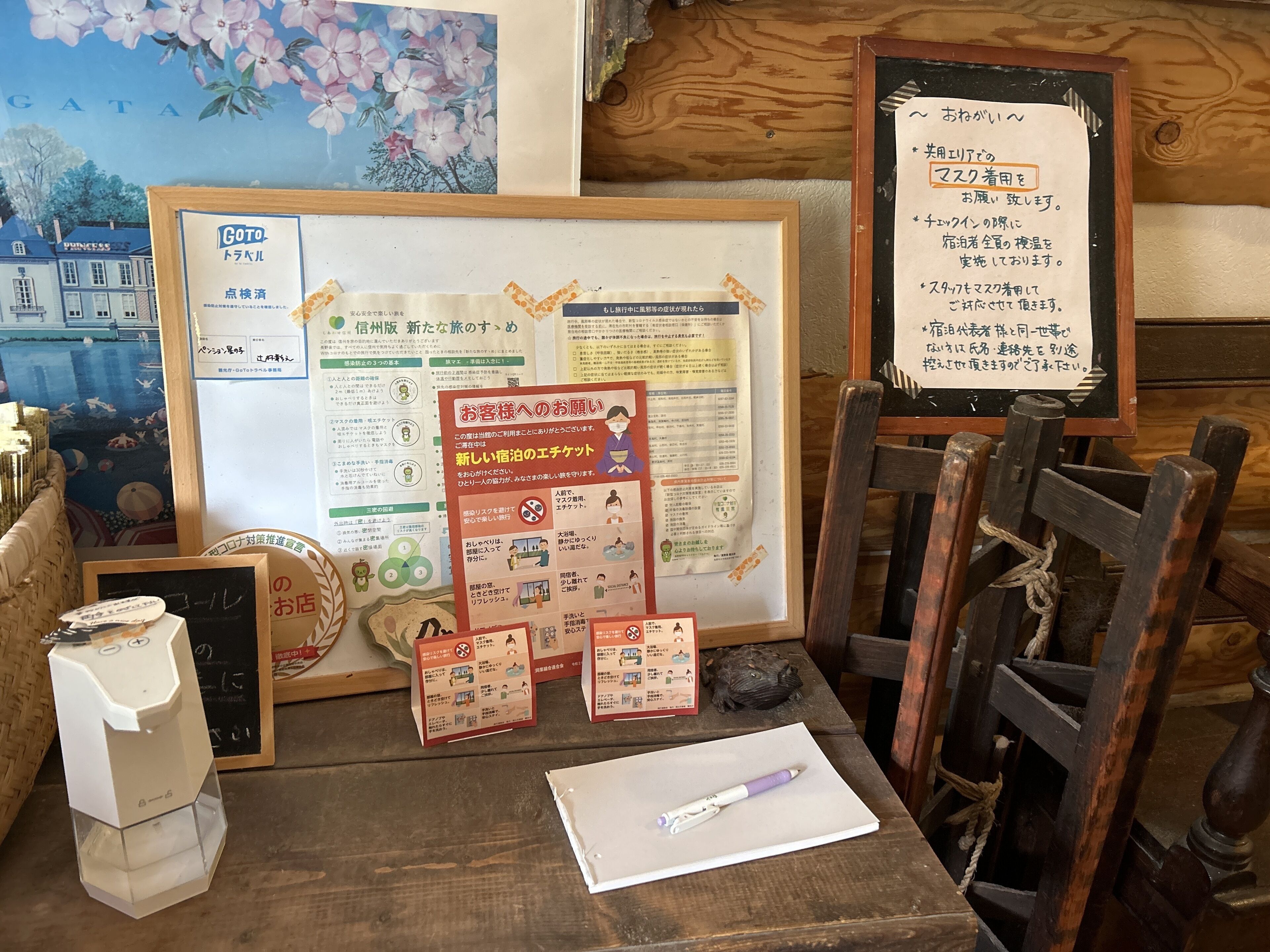 Uma mesa de madeira com vários cartazes informativos, um quadro emoldurado e uma pequena lousa com anotações manuscritas.