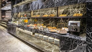 Um balcão de buffet com painel de mármore, diversos alimentos e uma máquina de café.