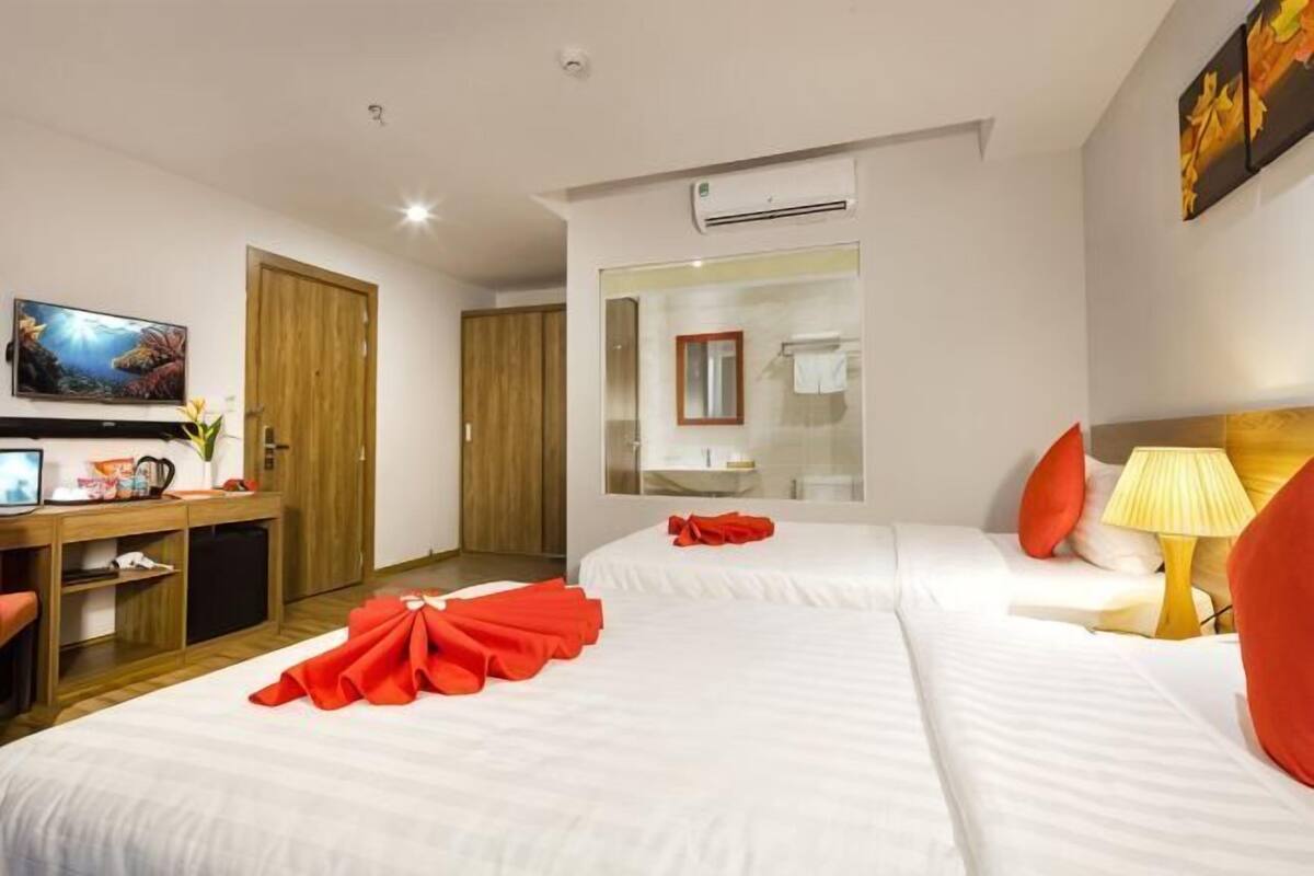 Quarto de hotel com duas camas, uma escrivaninha com computador, uma televisão e um espelho.