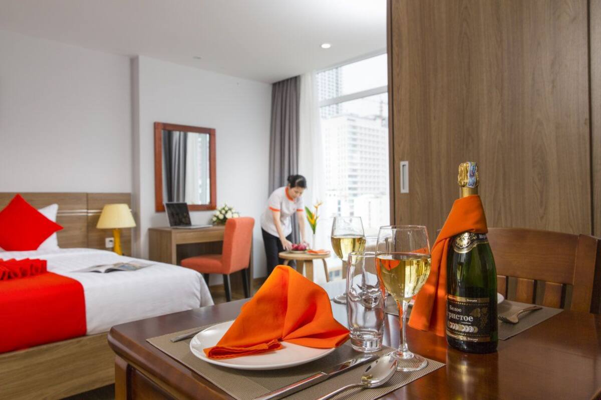 Quarto de hotel com uma cama, uma mesa de jantar com champanhe, copos e um prato.