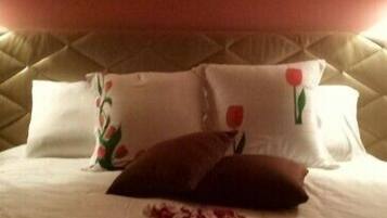 Uma cama com cabeceira acolchoada, duas almofadas com estampas florais e uma almofada escura.