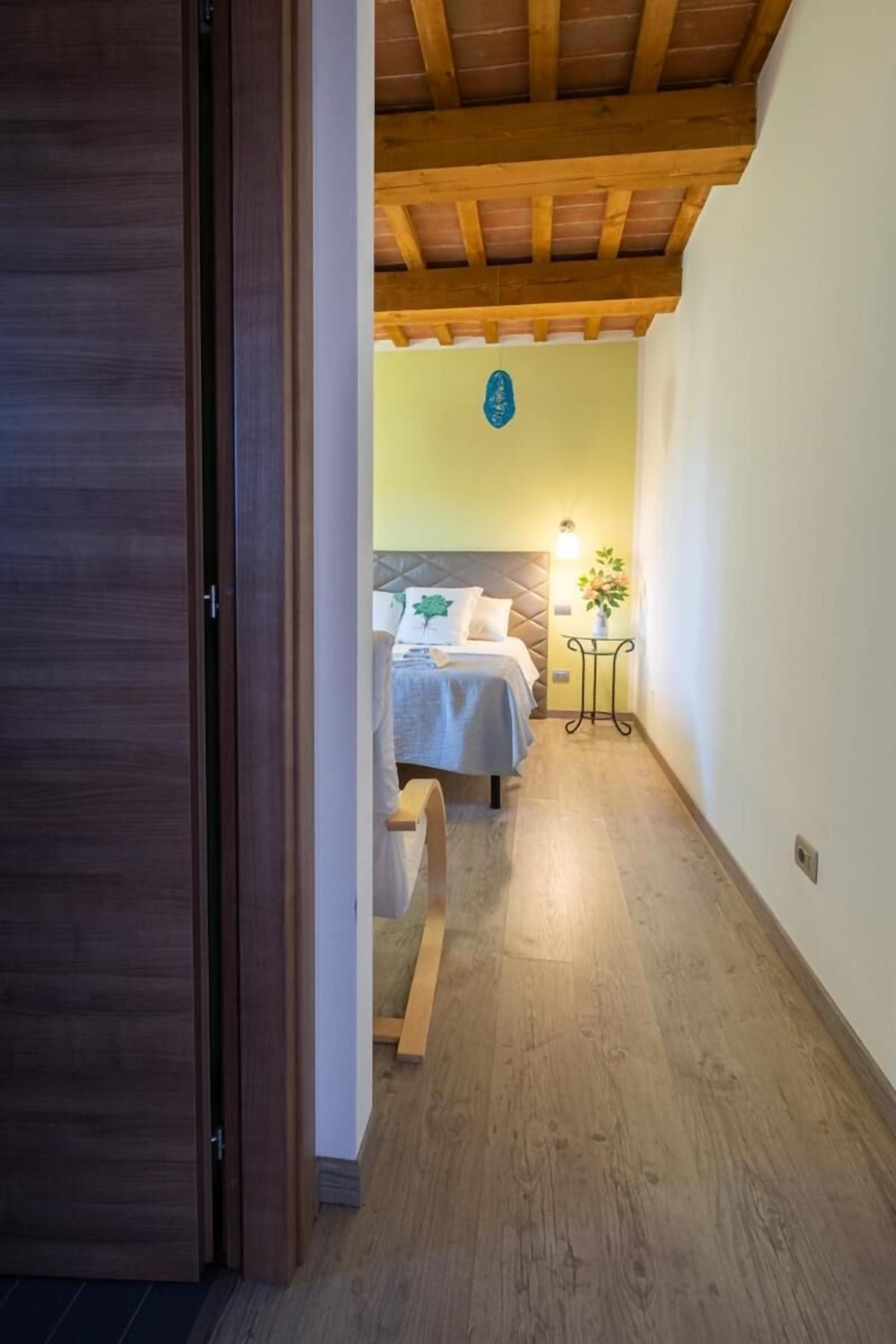 Um corredor estreito que dá para um quarto com teto de madeira e uma cama com cabeceira.