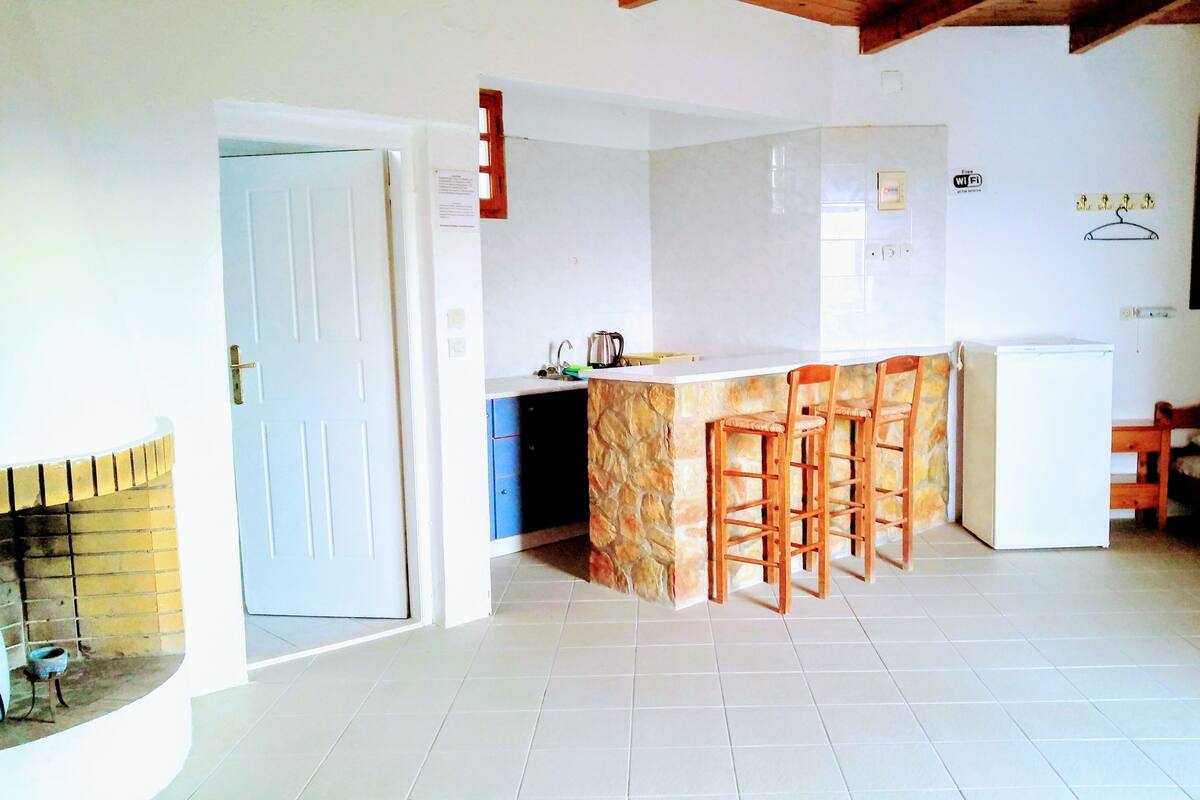 Uma cozinha compacta com uma ilha central, um frigorífico pequeno e uma área de refeições com cadeiras de madeira.