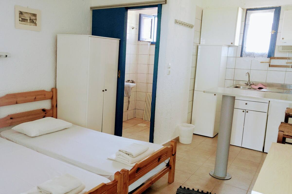 Quarto com cama, cabeceira de madeira, guarda-roupa e banheiro visível por uma porta aberta.