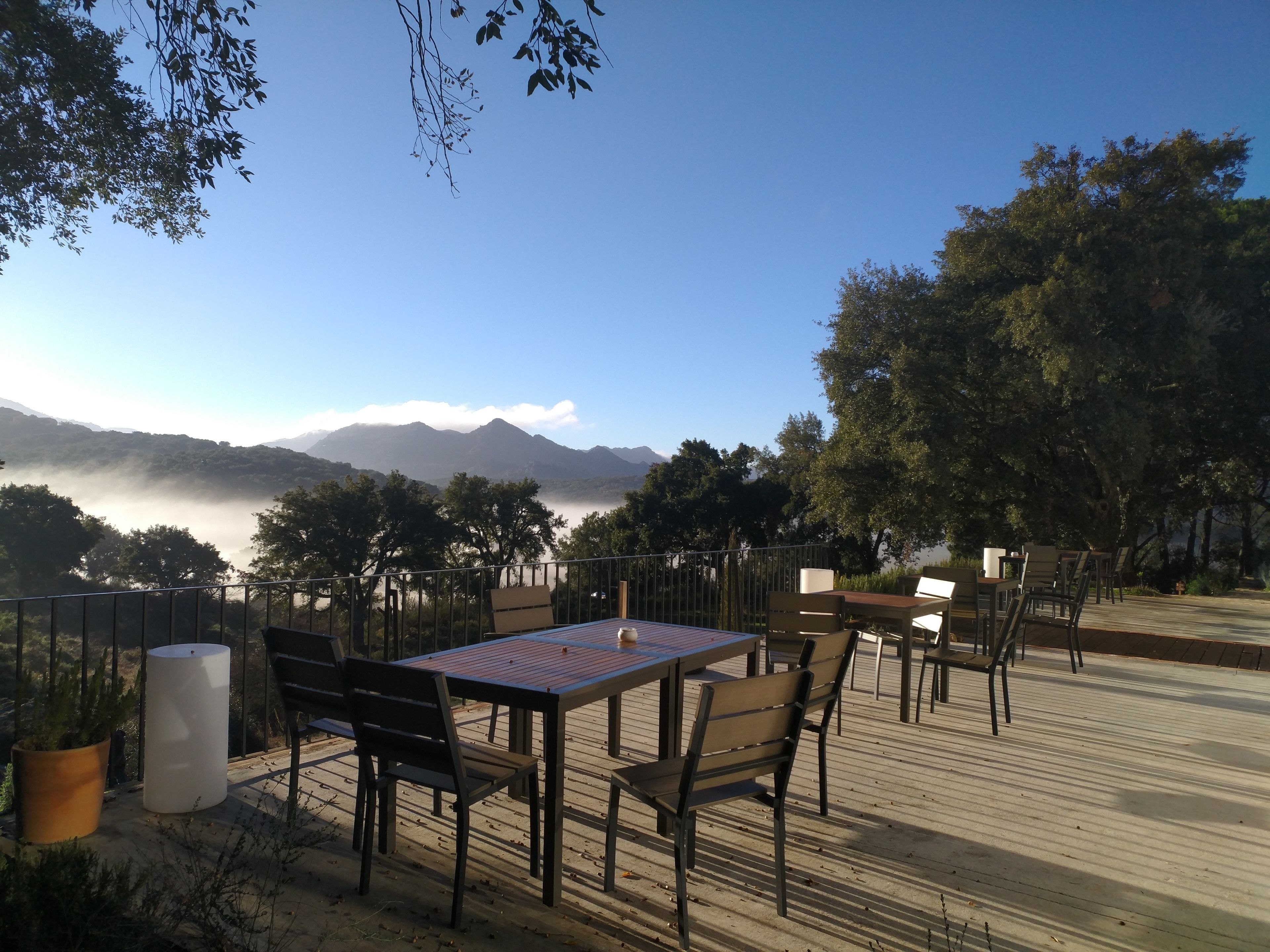 Uma área de refeições ao ar livre com mesa e cadeiras, com vista para um corpo de água e montanhas.