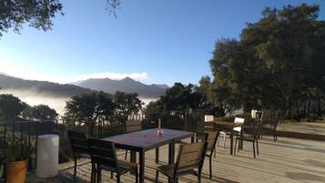 Uma área de refeições ao ar livre com mesa e cadeiras, com vista para um corpo de água e montanhas.