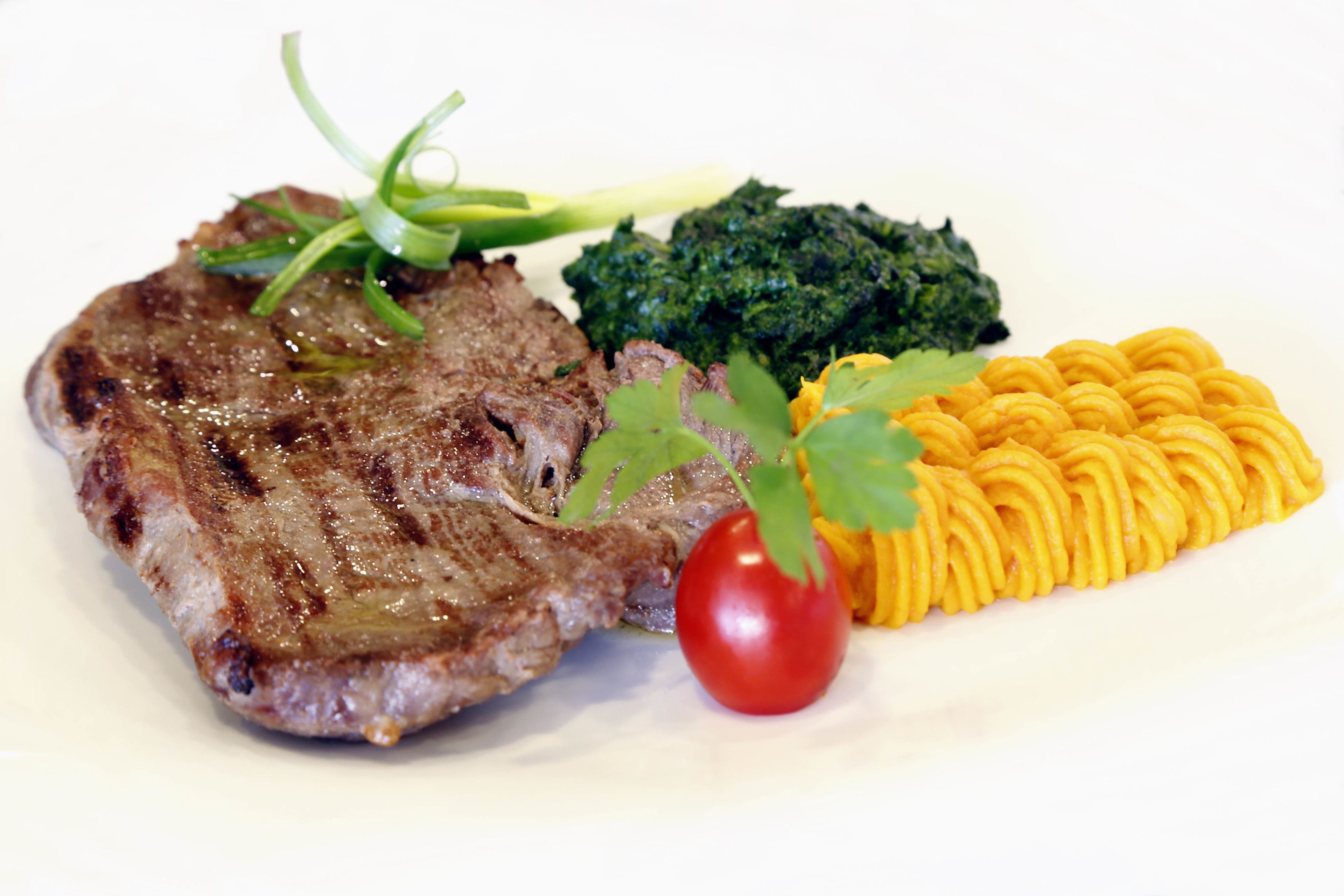 Prato com bife, brócolis, tomate cereja e massa amarela como acompanhamento.