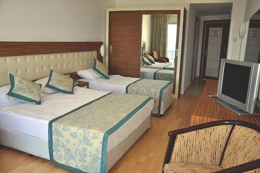 Quarto de hotel com duas camas, uma televisão e uma cadeira.