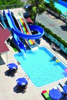 Um parque aquático com um tobogã de águas colorido, uma piscina e espreguiçadeiras com guarda-sóis.