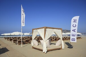Cenário de praia com cama de dossel e cadeiras de descanso.