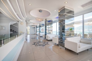 Um hall de hotel moderno com escadaria de vidro, sofás brancos e vista para a cidade.