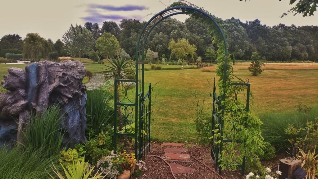 Um jardim com um arco de metal, um toco de árvore grande e um caminho que leva a um campo gramado.