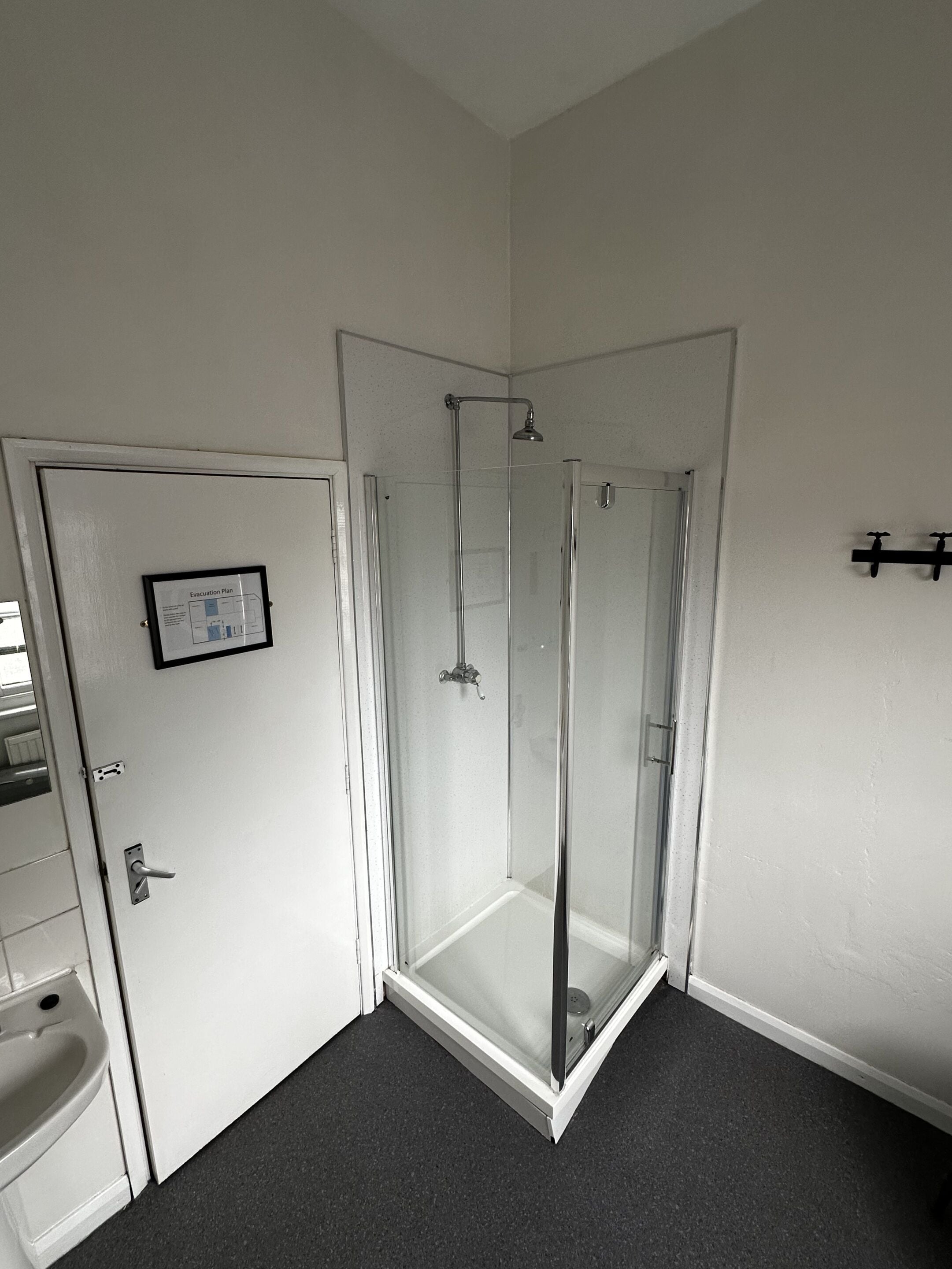 Casa de banho nos cantos, com cabine de duche em vidro, porta branca com um aviso emoldurado, e um porta-toalhas preto na parede.