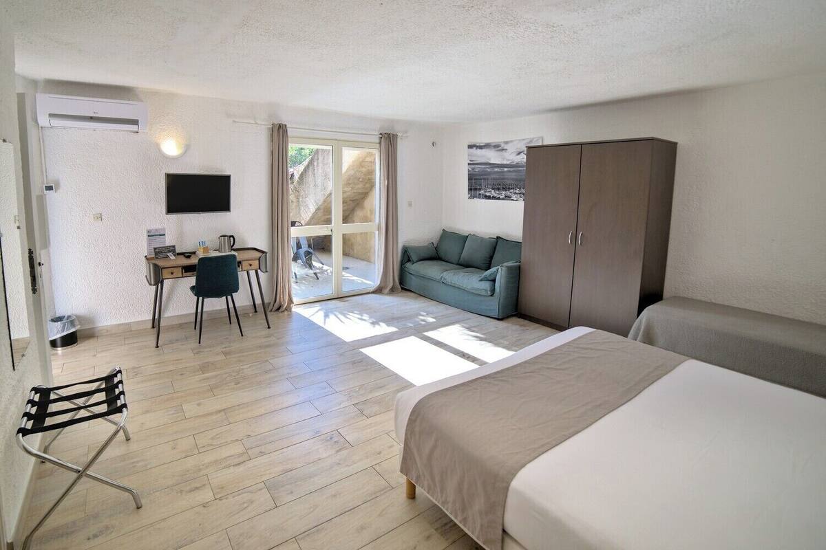 Quarto com cama, escrivaninha com cadeira, sofá e guarda-roupa. Porta de vidro deslizante dá acesso a uma área externa.