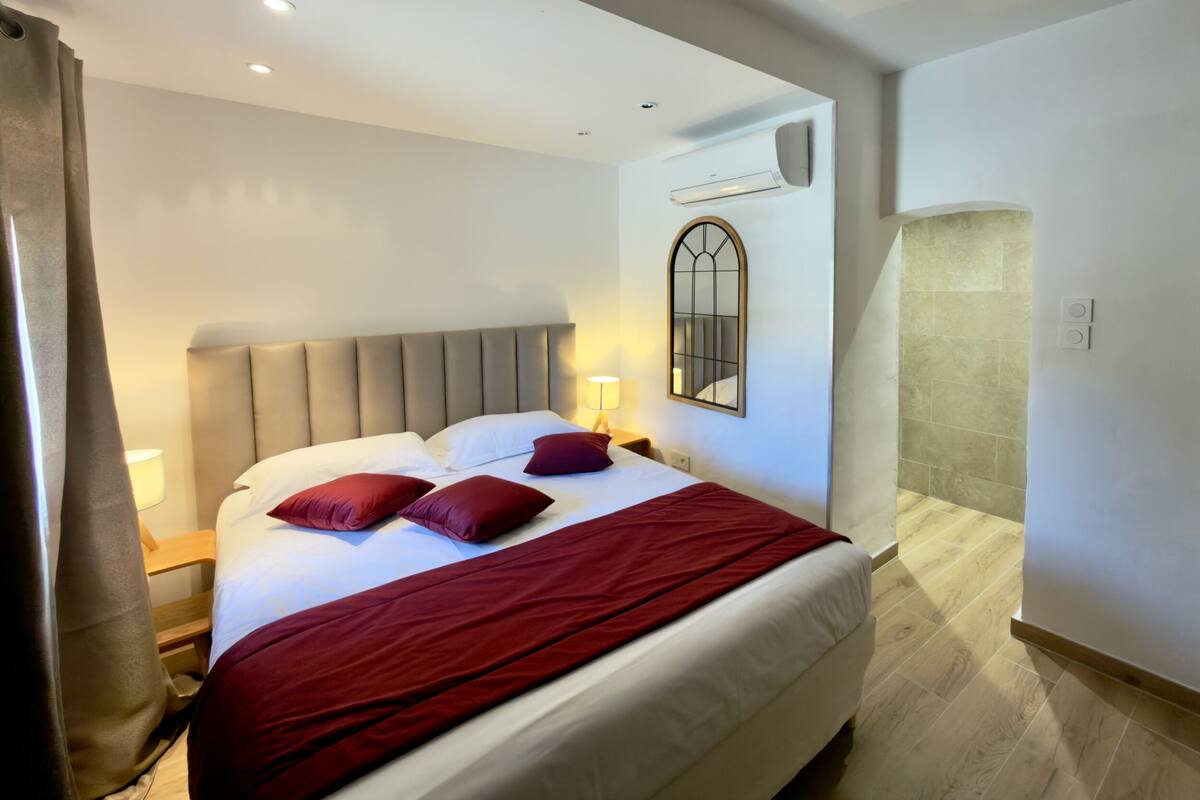 Quarto de hotel com cama, mesa de cabeceira, abajur, espelho e ar condicionado.