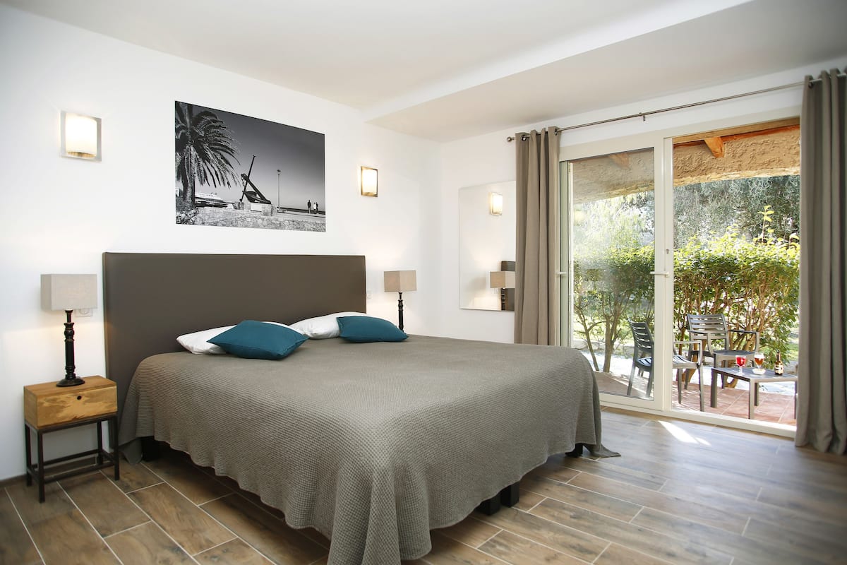 Quarto com cama, mesas de cabeceira e uma grande janela com vista para o verde.