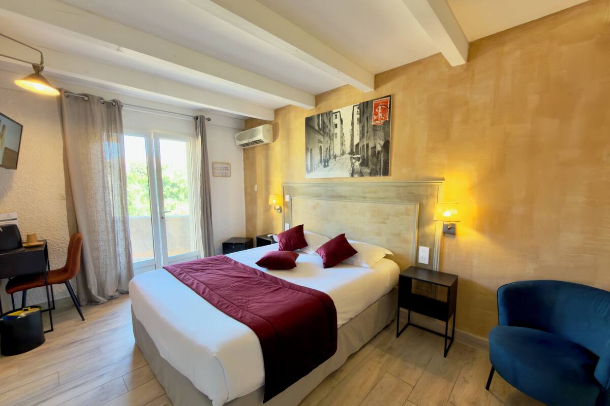 Quarto de hotel com cama, escrivaninha, cadeira e vista para o exterior.