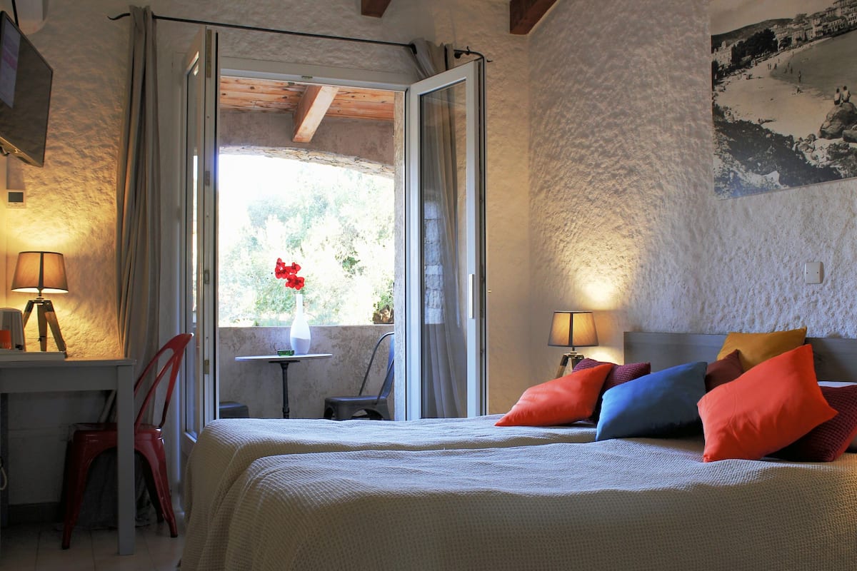 Quarto com cama, duas luminárias de apoio, uma cadeira, uma mesa e uma janela com cortinas.