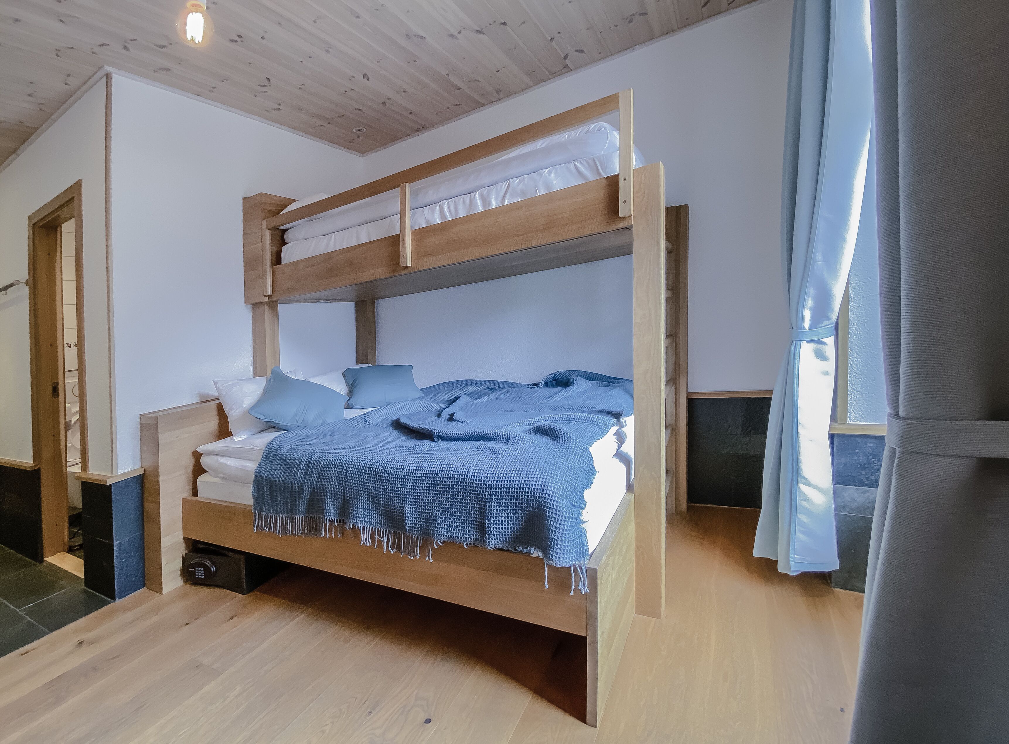 Uma cama de beliche com cobertor e travesseiros azuis, cabeceira de madeira e uma pequena mesa de cabeceira com abajur.