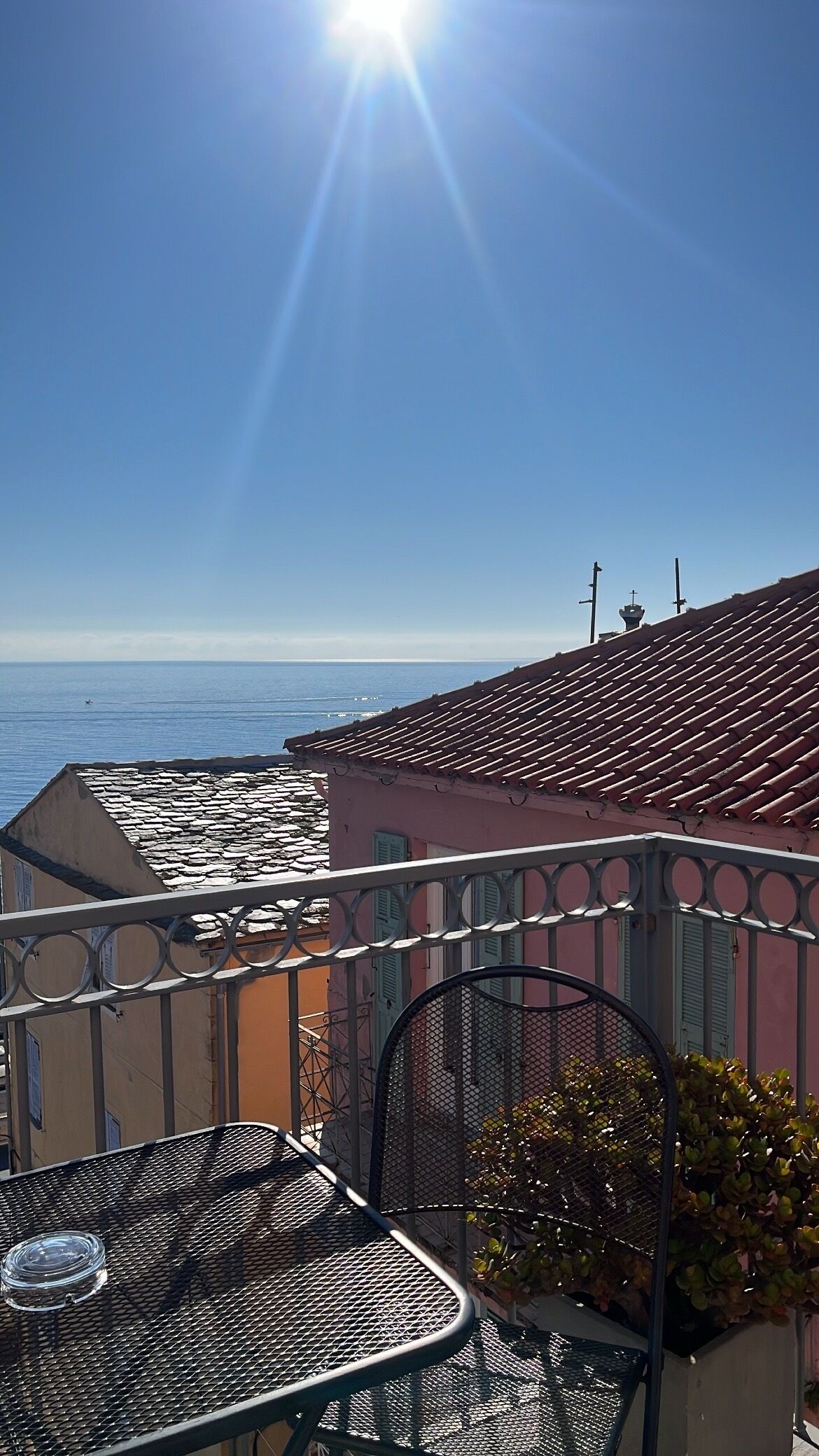 Terraço com mesa e cadeiras, vista para a costa, edifícios e céu limpo.