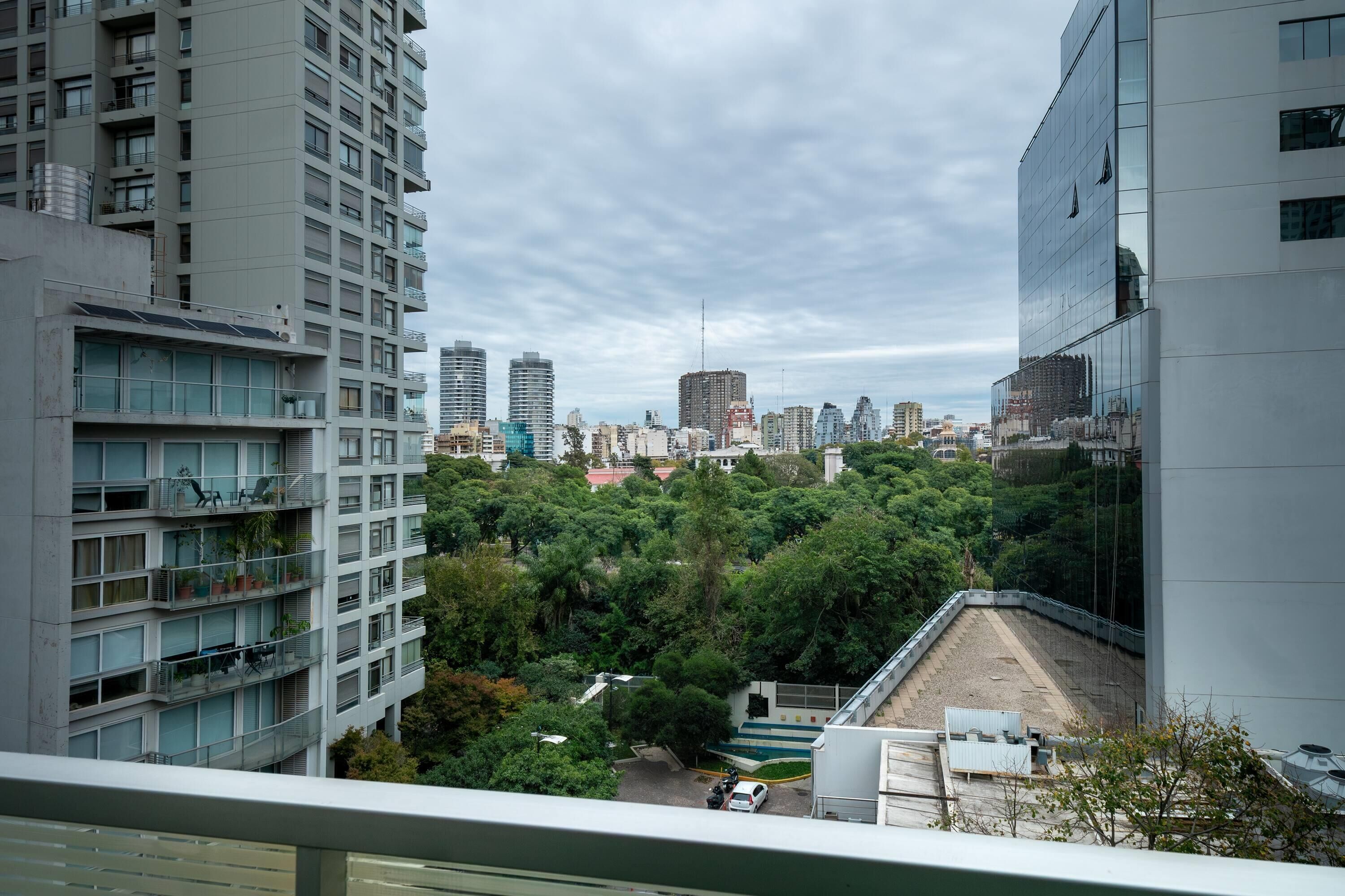 Um edifício alto com várias varandas, área de estacionamento e vista para um horizonte urbano com diversos edifícios e áreas verdes.