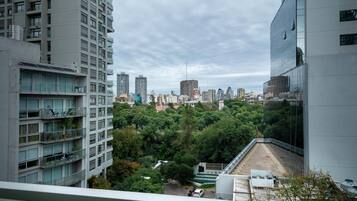 Um edifício alto com várias varandas, área de estacionamento e vista para um horizonte urbano com diversos edifícios e áreas verdes.