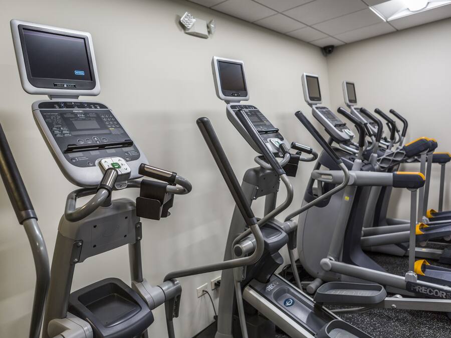 Várias passadeiras laterais com mostradores digitais e painéis de comando, em um ginásio.