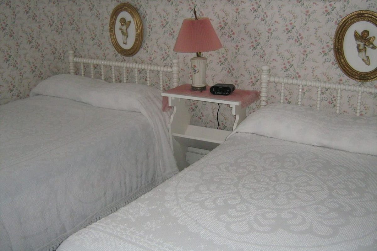 Quarto com duas camas de solteiro, mesa de cabeceira com abajur e papel de parede floral.