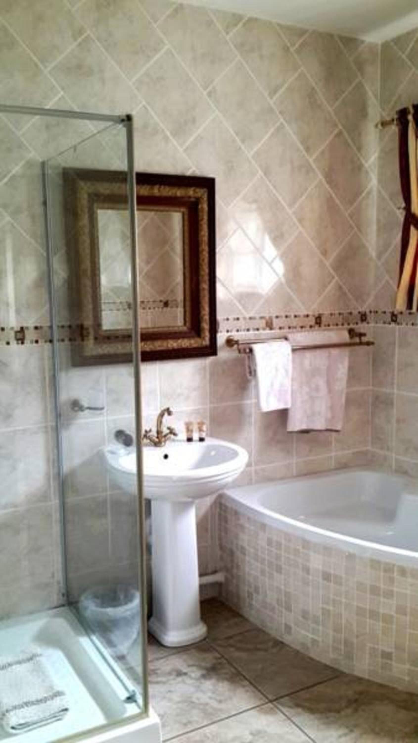 Casa de banho com cabine de chuveiro em vidro, lavatório suspenso, banheira e parede revestida com bordadura decorativa.