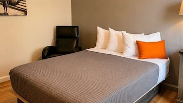 Quarto de hotel com uma cama grande, uma poltrona, uma mesa de cabeceira e um quadro na parede.