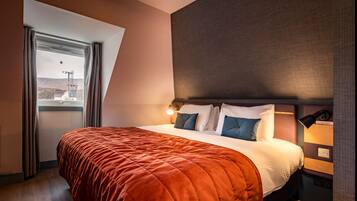 Quarto de hotel moderno com uma cama grande, vista para o exterior e mesa de cabeceira com abajur.