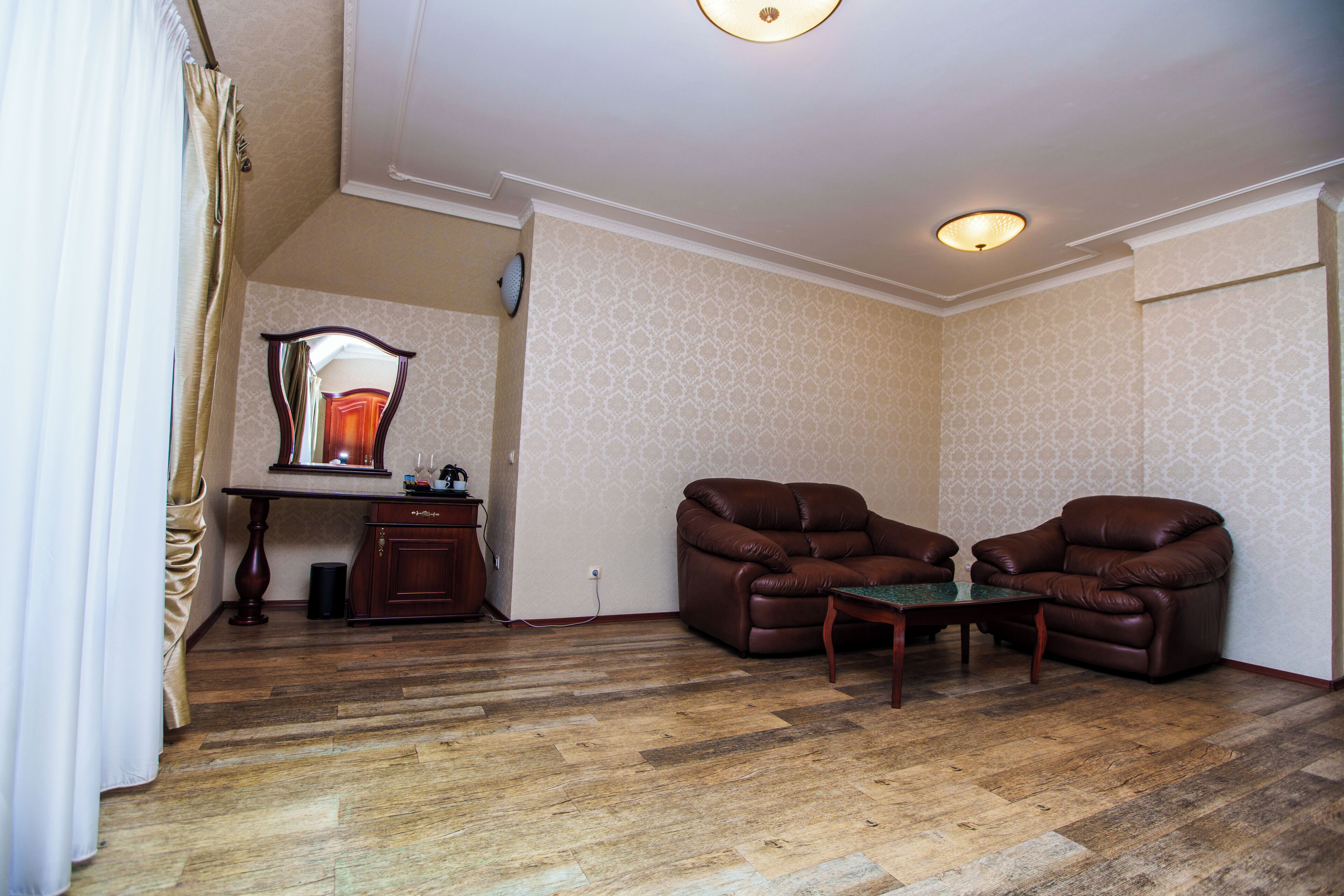 Quarto com piso de madeira, dois poltronas de couro, uma mesinha, um espelho e uma porta.