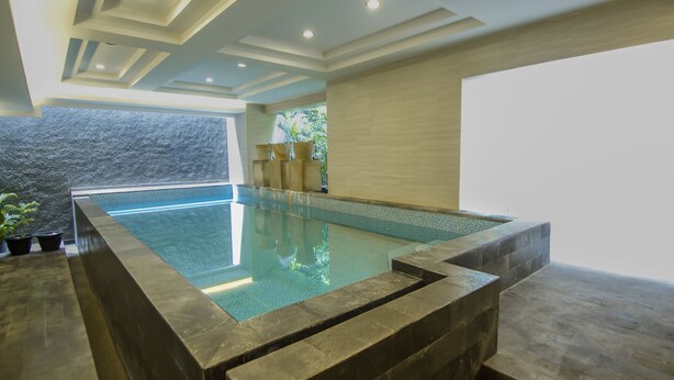 Piscina interior moderna com parede de pedra e plantas em vasos.