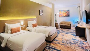 Quarto de hotel com duas camas, um sofá, uma escrivaninha e uma televisão.