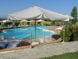Uma área de piscina com guarda-sóis brancos, espreguiçadeiras e um caminho de pedra.