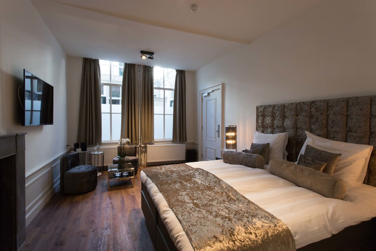 Quarto moderno com uma cama grande, televisão de tela plana, lareira e vista da cidade através de janelas amplas.