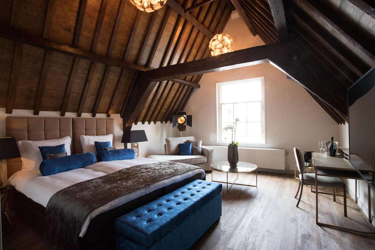 Quarto com cama grande, um banco, um sofá, uma mesa de jantar e uma janela.