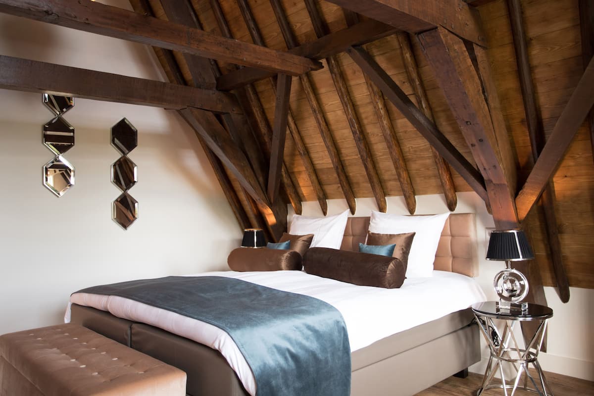 Quarto com teto de madeira, cama com colcha azul e mesa de cabeceira com abajur.
