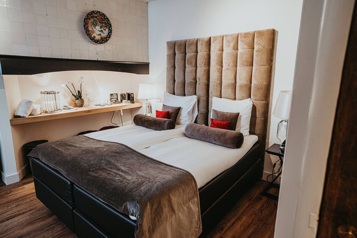 Quarto de hotel moderno com uma cama grande, uma mesinha de cabeceira e uma prateleira fixada na parede.