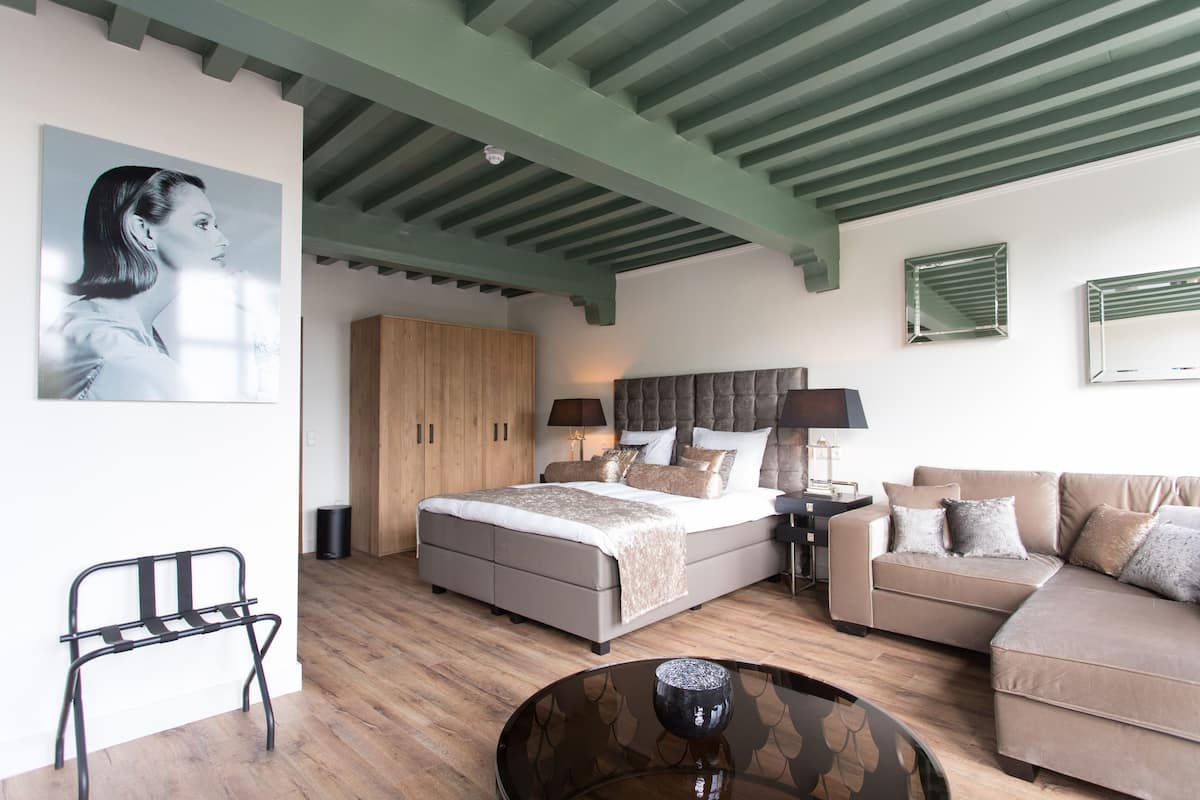 Quarto com cama, mesas de cabeceira, sofá, poltrona e um quadro na parede.