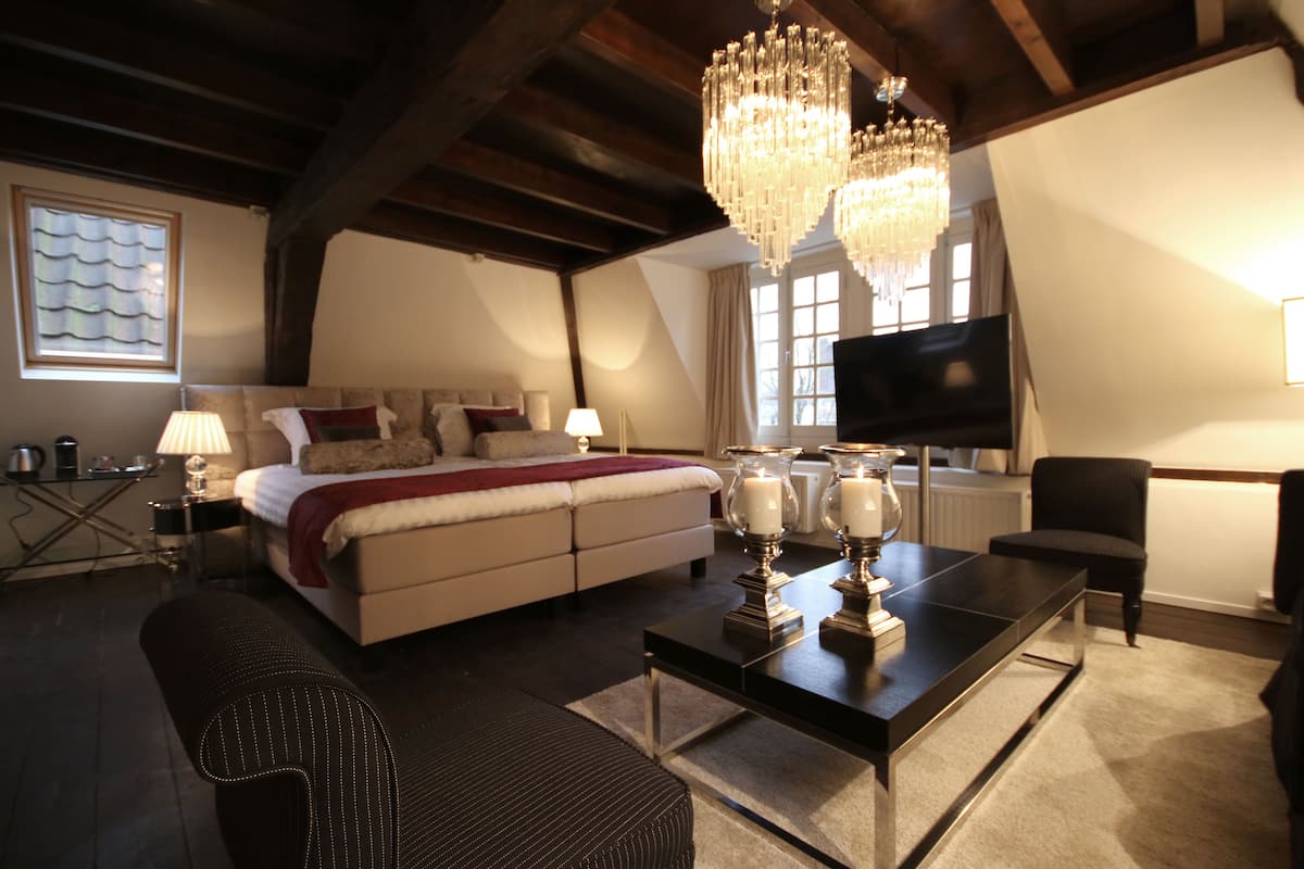 Quarto com cama, mesas de cabeceira, televisão e lustre.