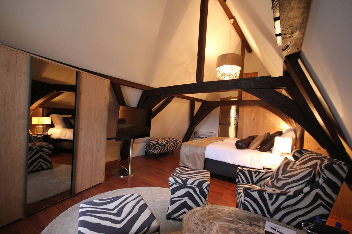 Um quarto aconchegante com uma cama, pufes com padrão de zebra, um espelho e um candelabro.