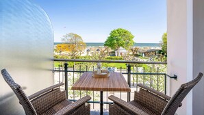 Varanda com móveis de vime, uma mesa e vista para o mar e edifícios.