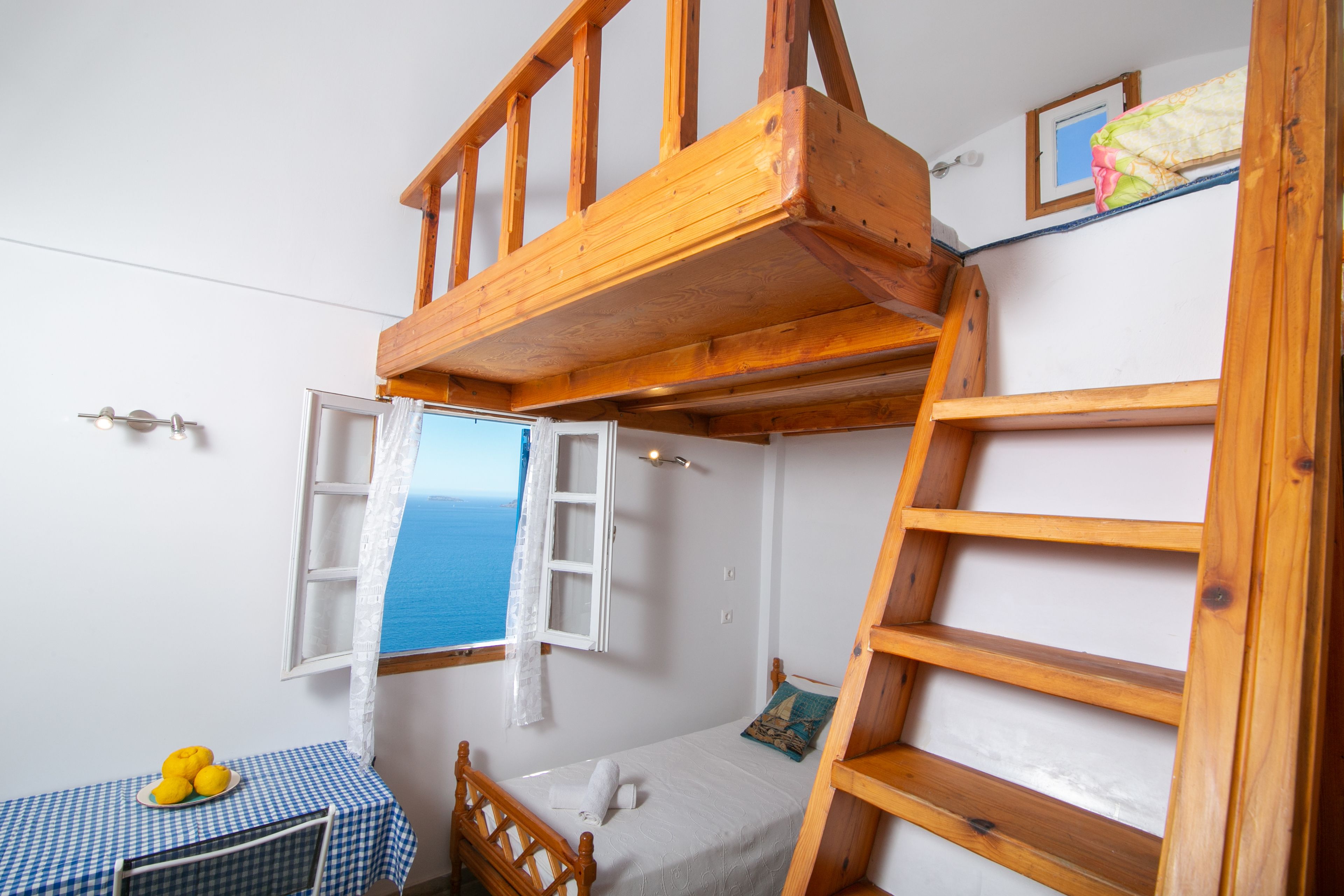 Quarto compacto com beliche, uma pequena mesa com limões e janela com vista para o mar.
