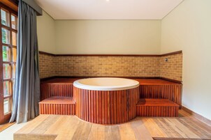 Quarto de canto com área de estar com banco de madeira e banheira de hidromassagem integrada.