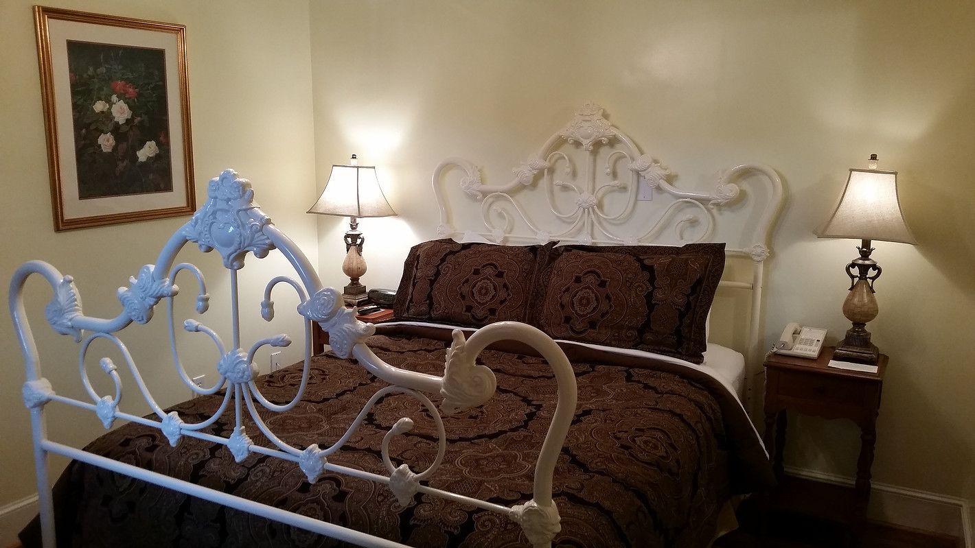 Quarto com cabeceira de metal decorativa, colcha estampada, duas luminárias de apoio e um quadro na parede.