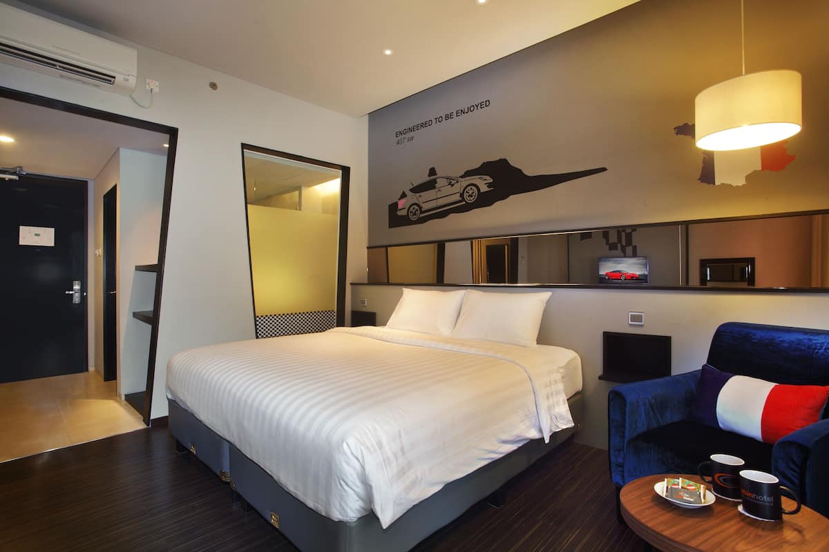 Quarto de hotel com cama, área de estar com mesa, televisão e parede com carro e texto.