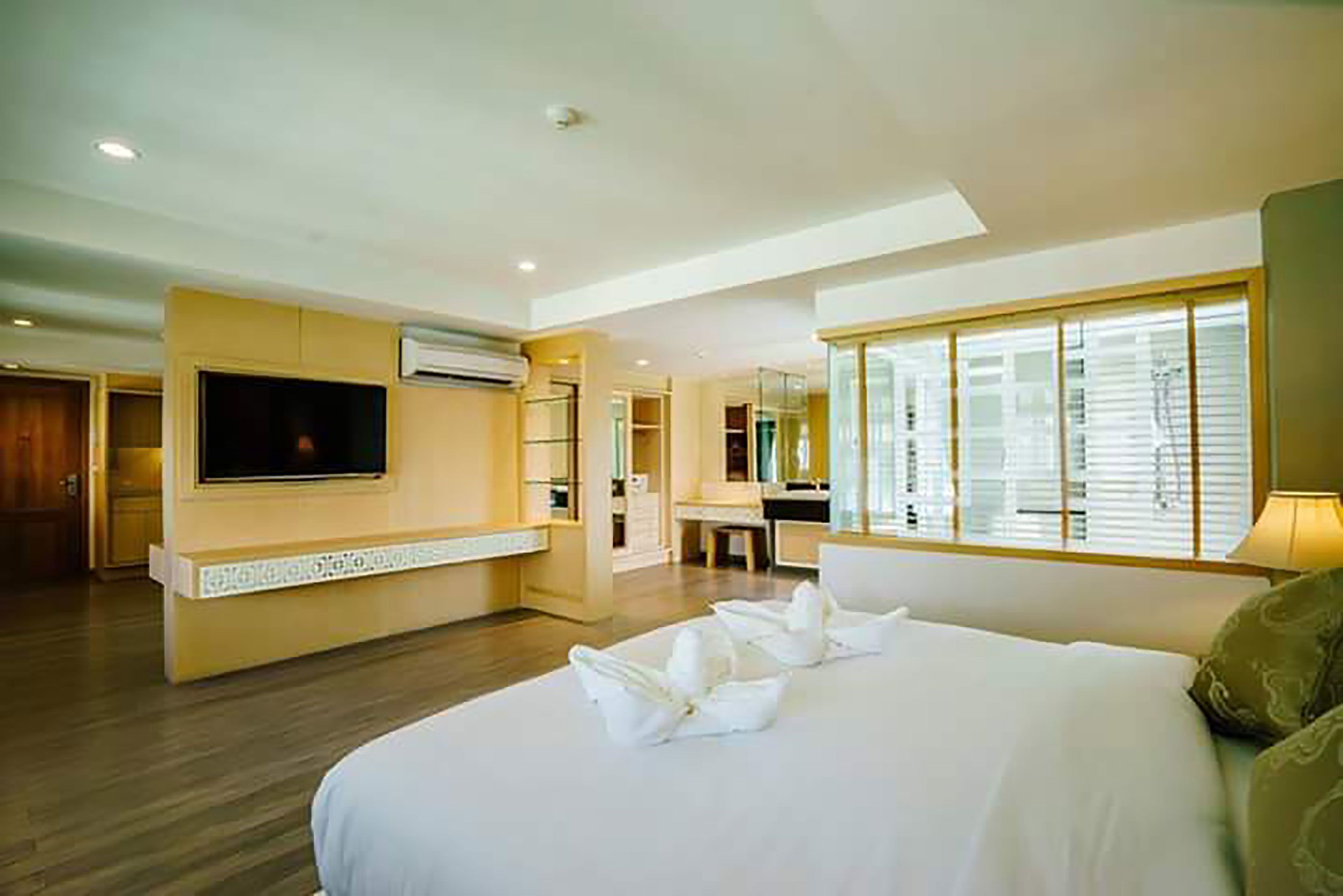 Quarto de hotel com uma cama grande, televisão de tela plana fixada na parede, uma escrivaninha e uma janela com persianas.